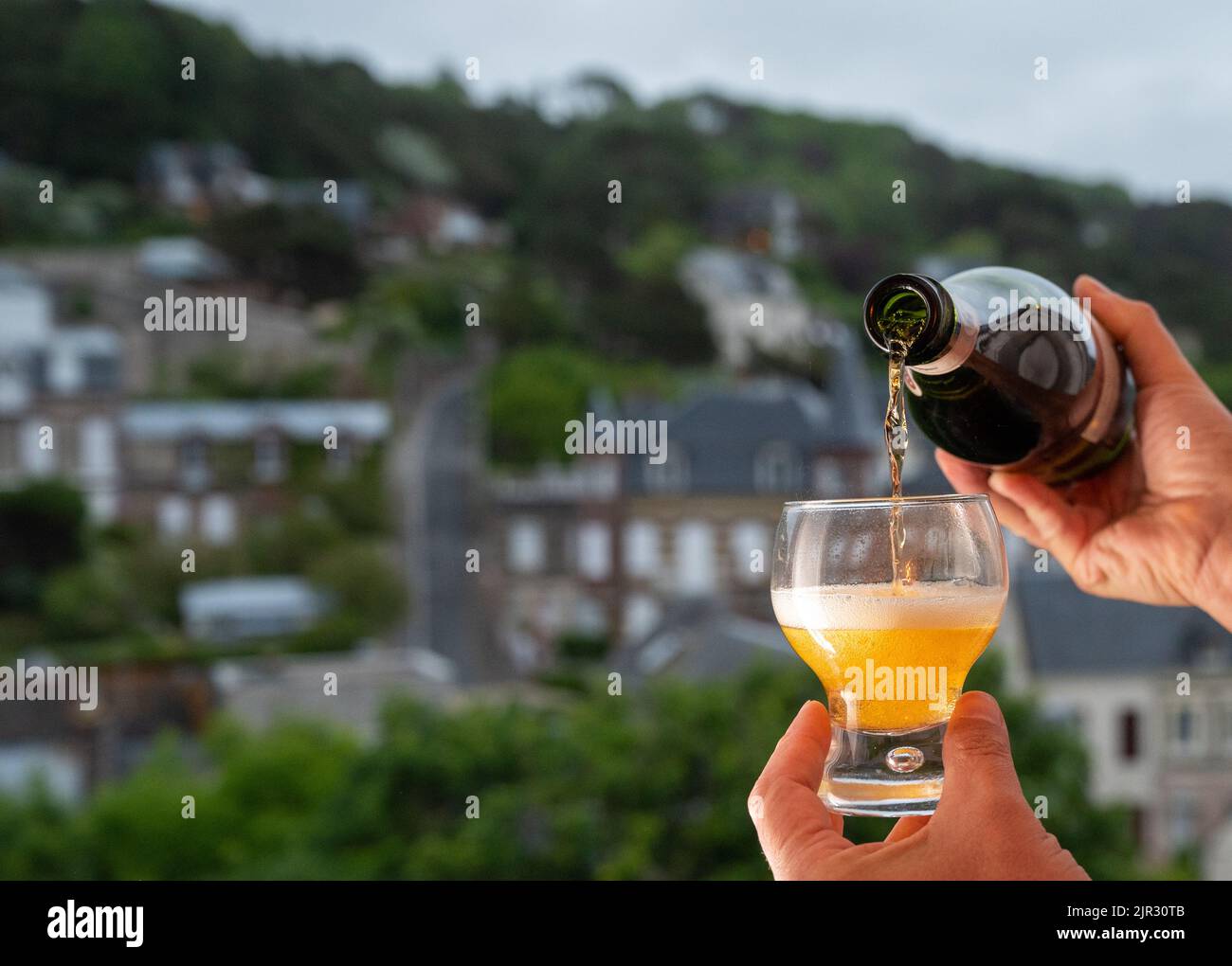 Pouring of tasty apple cider drink in glass with houses of Etretat ...