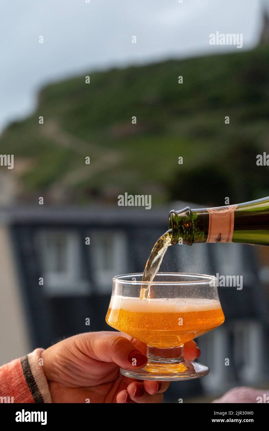 Pouring of tasty apple cider drink in glass with houses of Etretat ...
