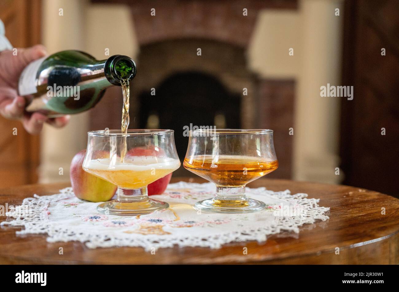 Pouring of apple cider drink in two glasses in old french house with ...