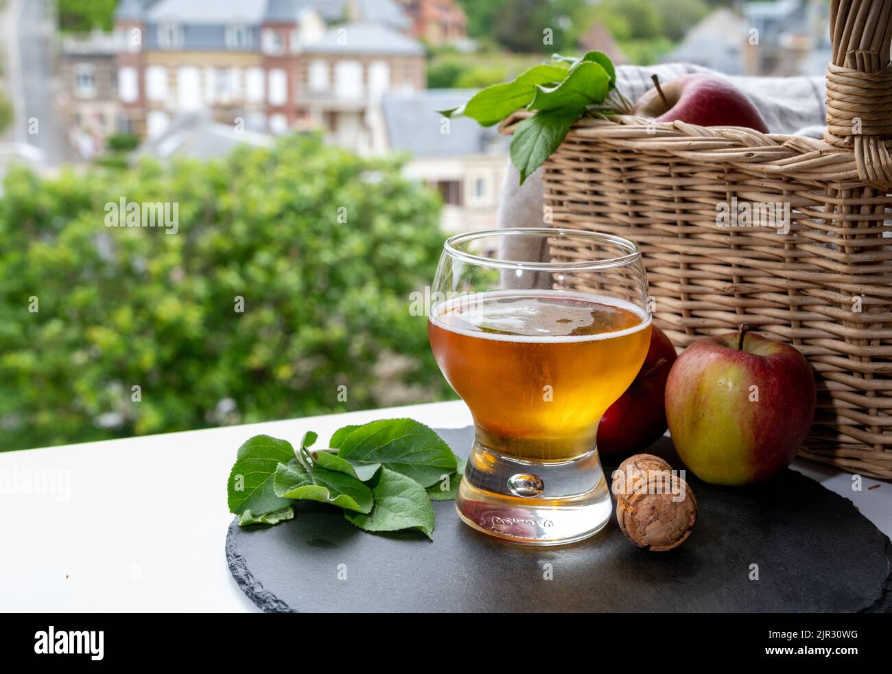 Glass of cold apple cider drink, ripe apples with leaves and houses of ...