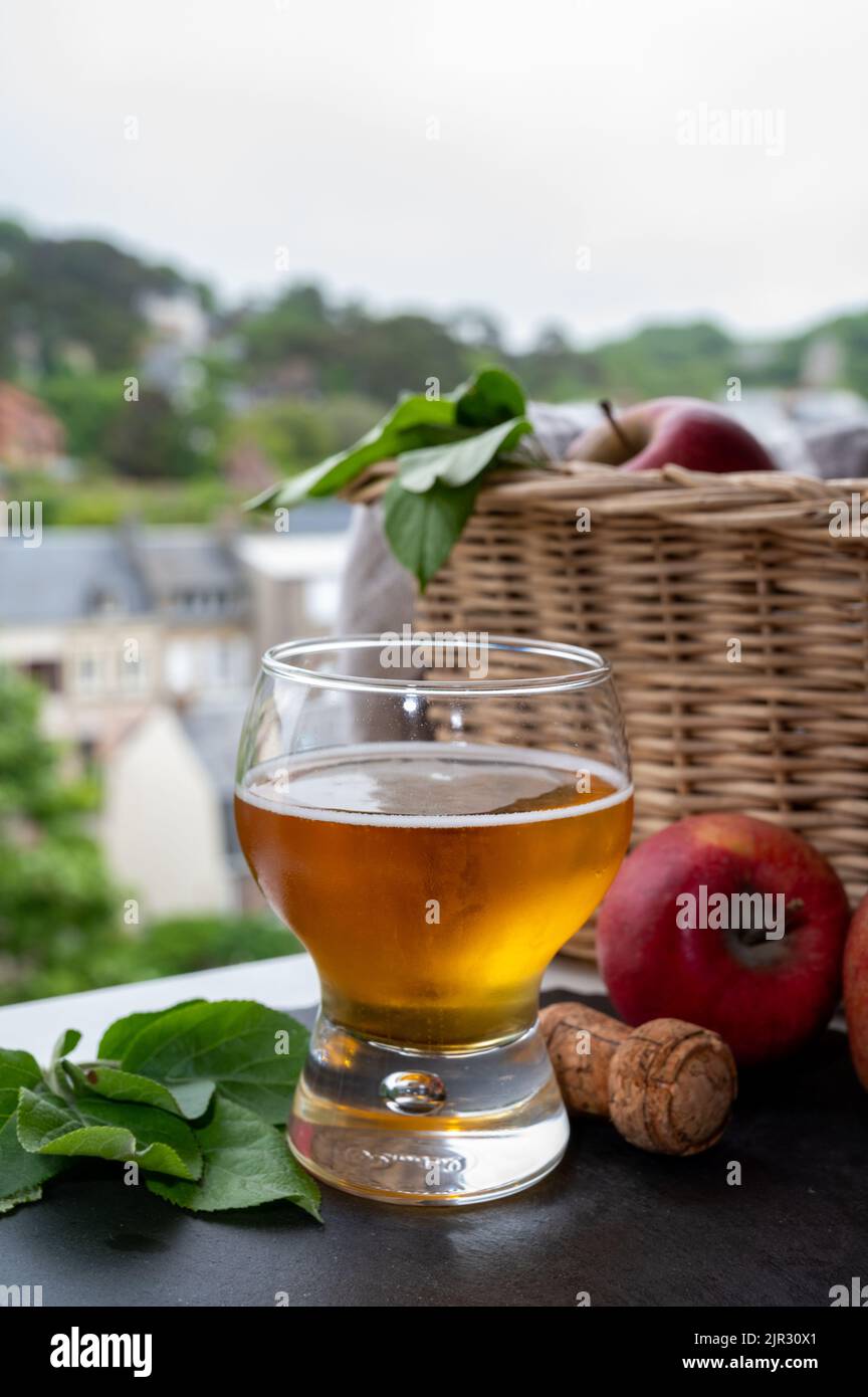 Glass of cold apple cider drink, ripe apples with leaves and houses of ...