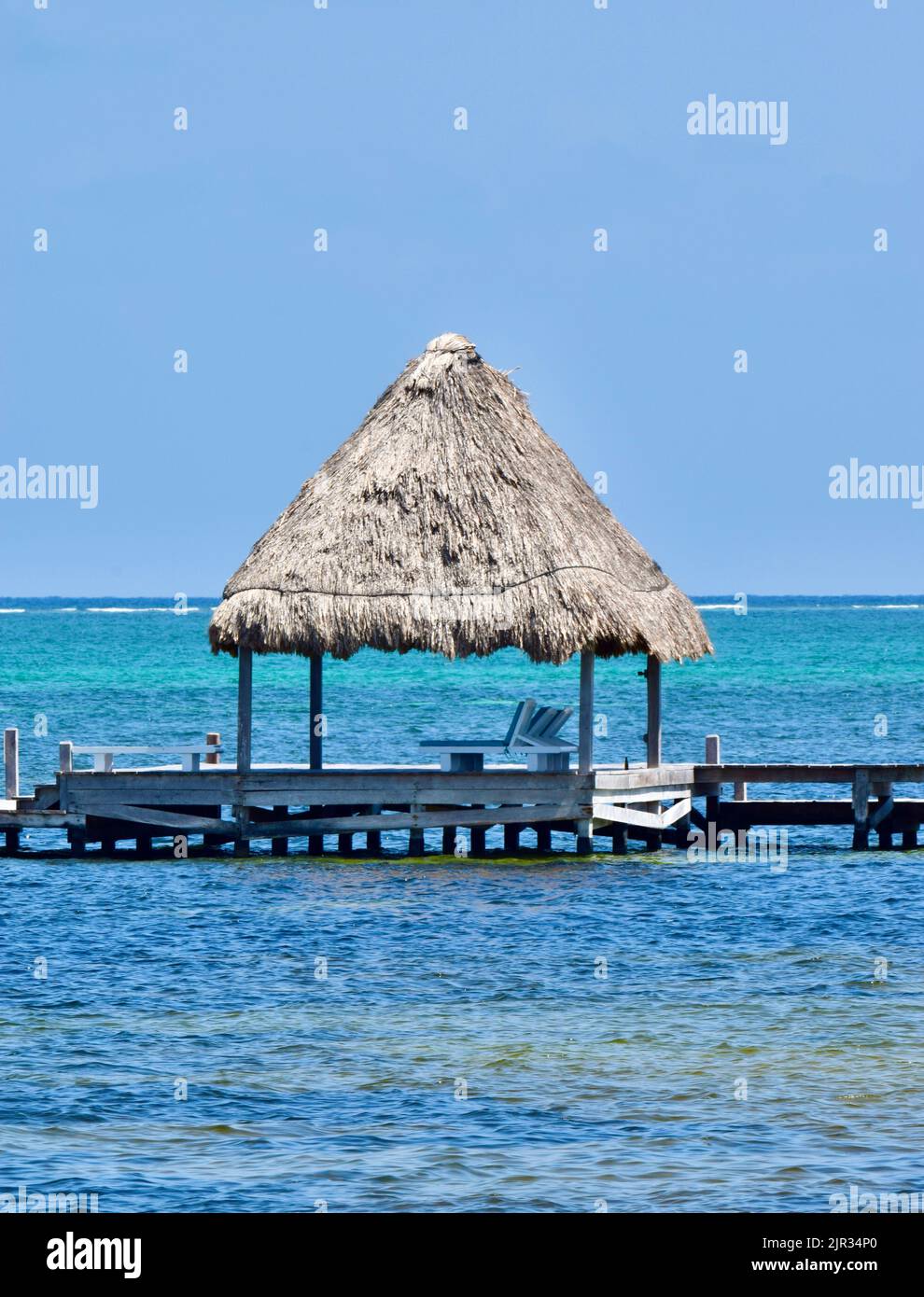 Some lounge chairs under a palapa on a pier over blue water on ...