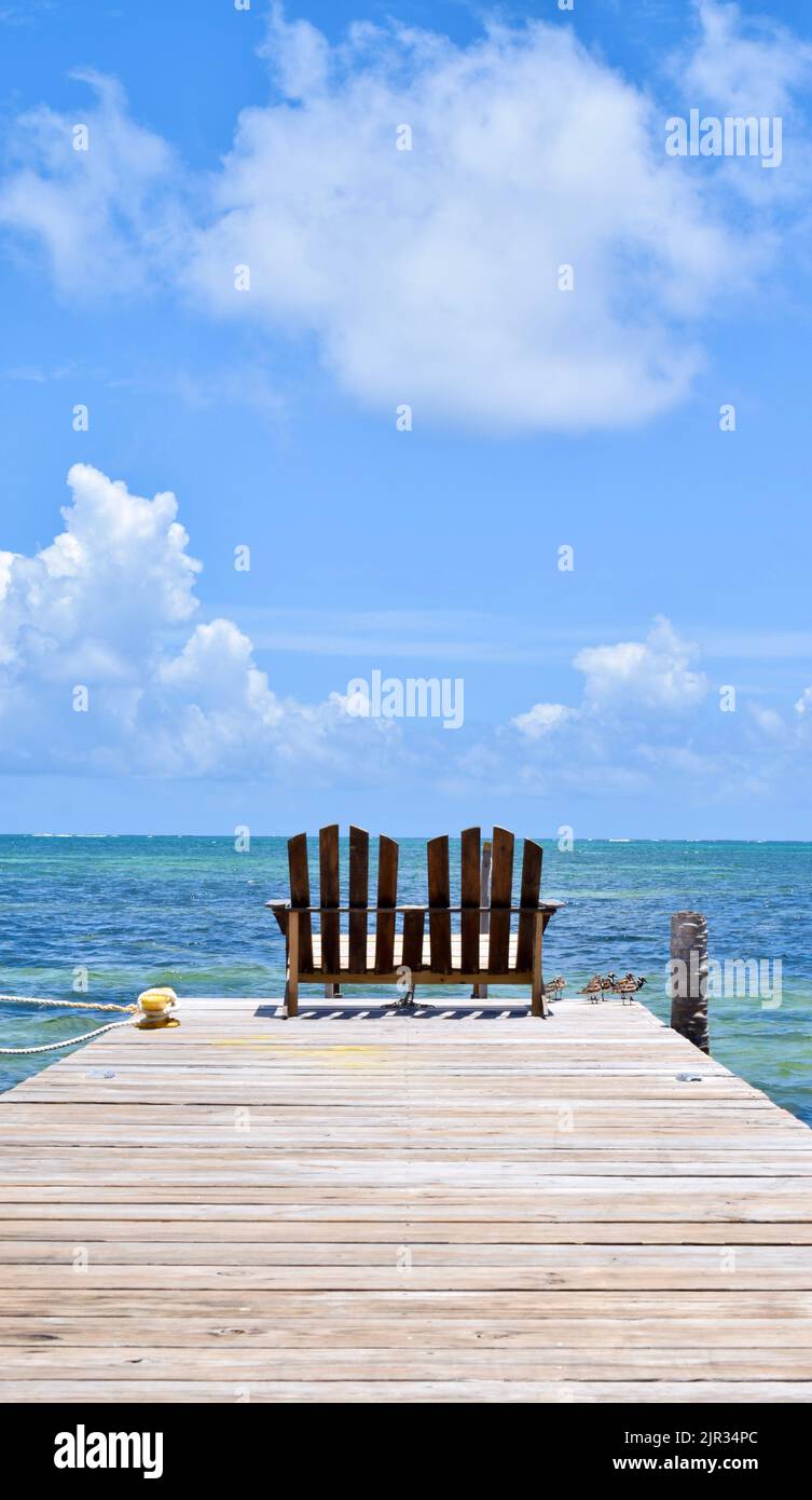 A pair of wooden chairs at the end of a pier on a calm, clear day on ...