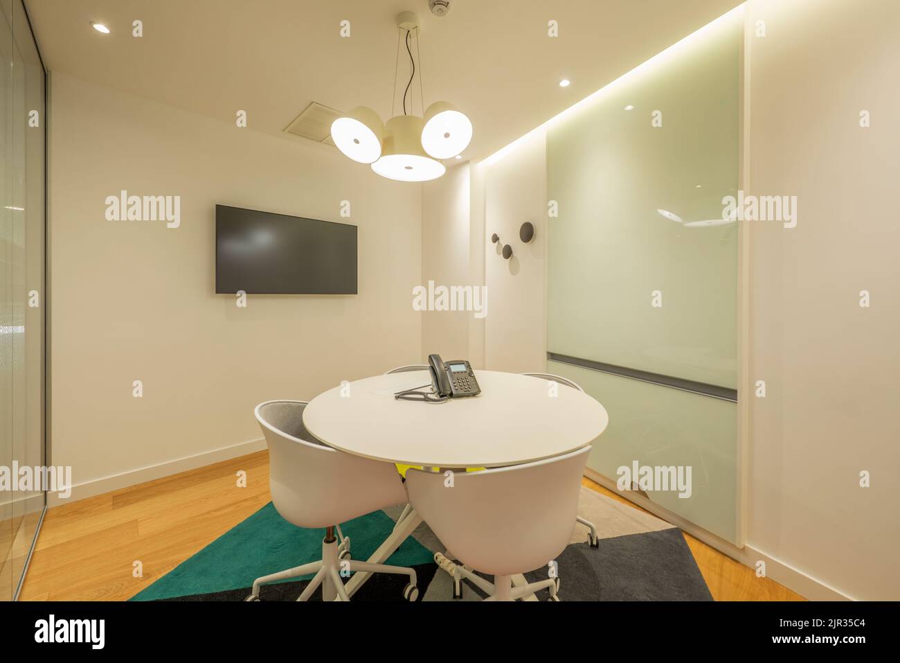Office cubicle with round table, white swivel chairs, tv on the wall ...