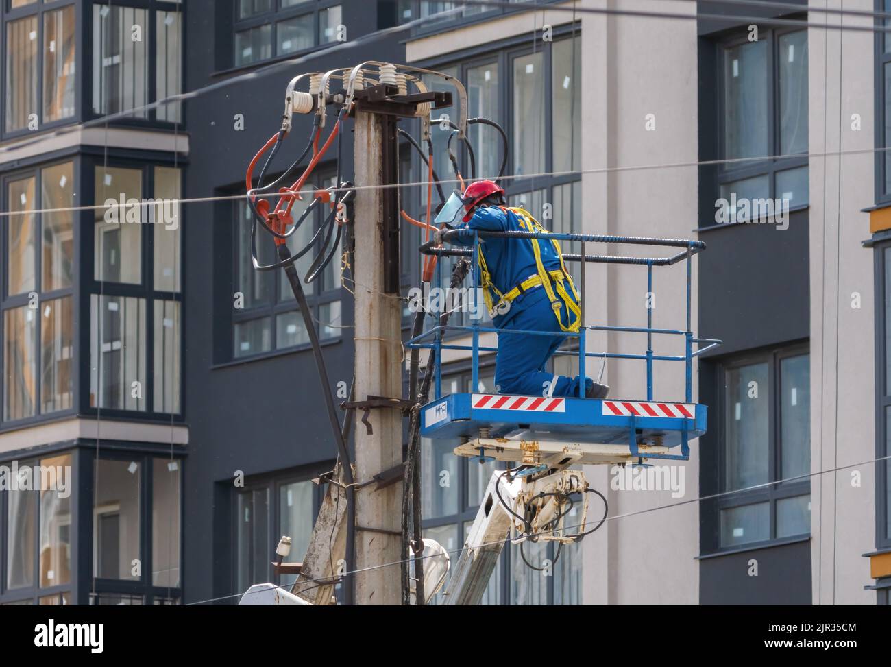 An electrician raised in the cradle of a tower lift mounts wires on a ...