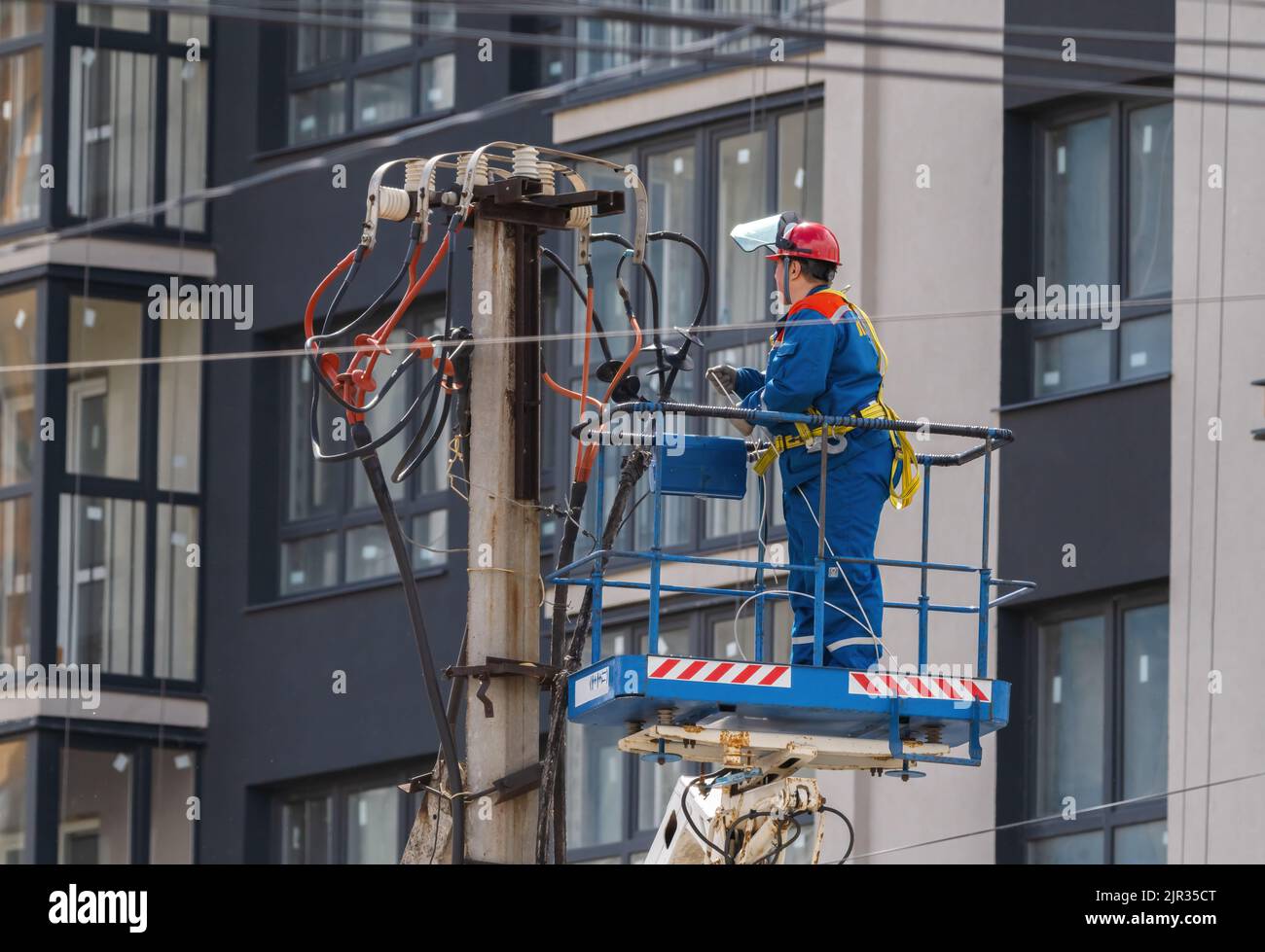 An electrician raised in the cradle of a tower lift mounts wires on a ...
