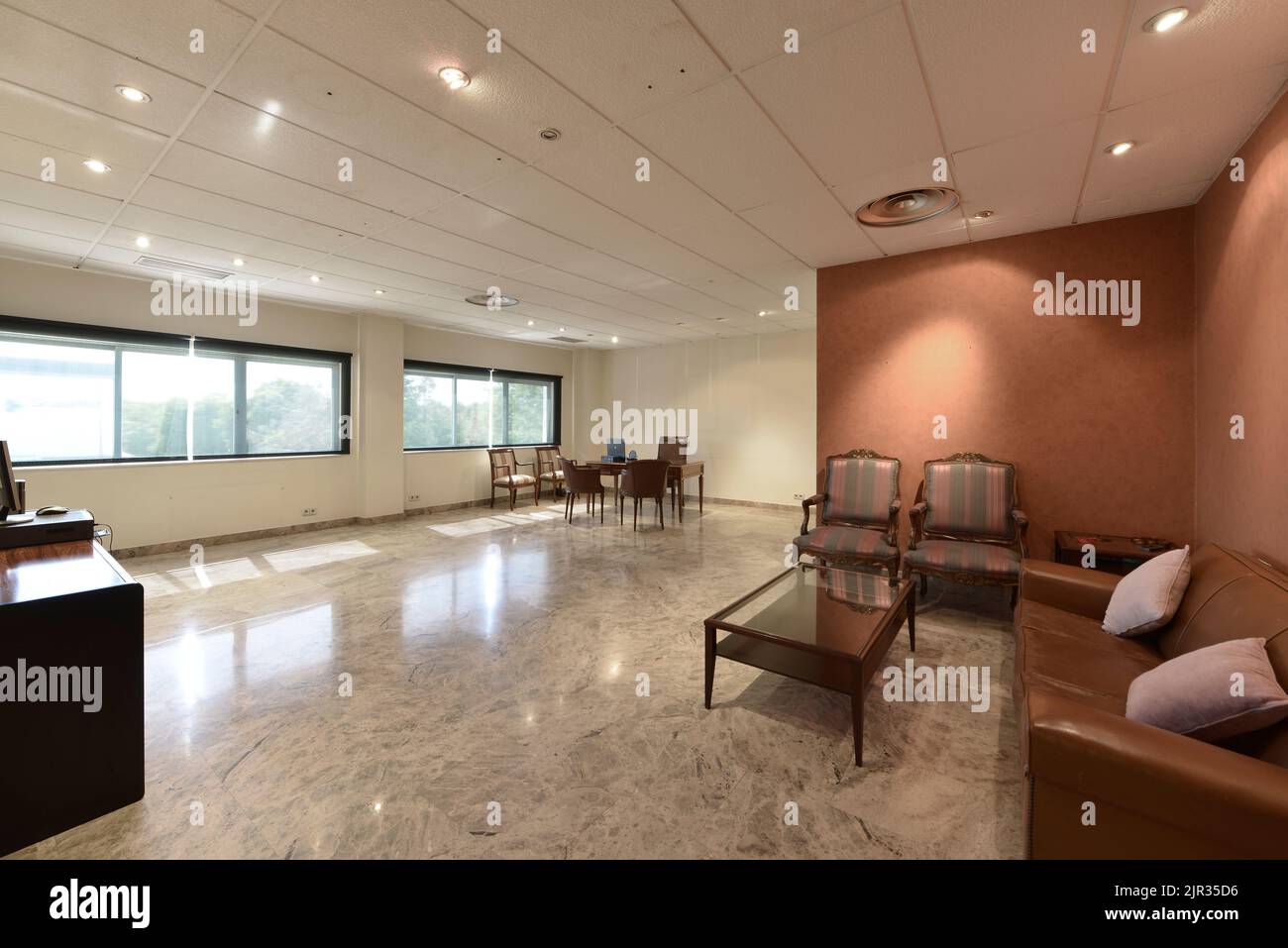 Large semi-empty room with brown leather sofas, wooden armchairs with ...