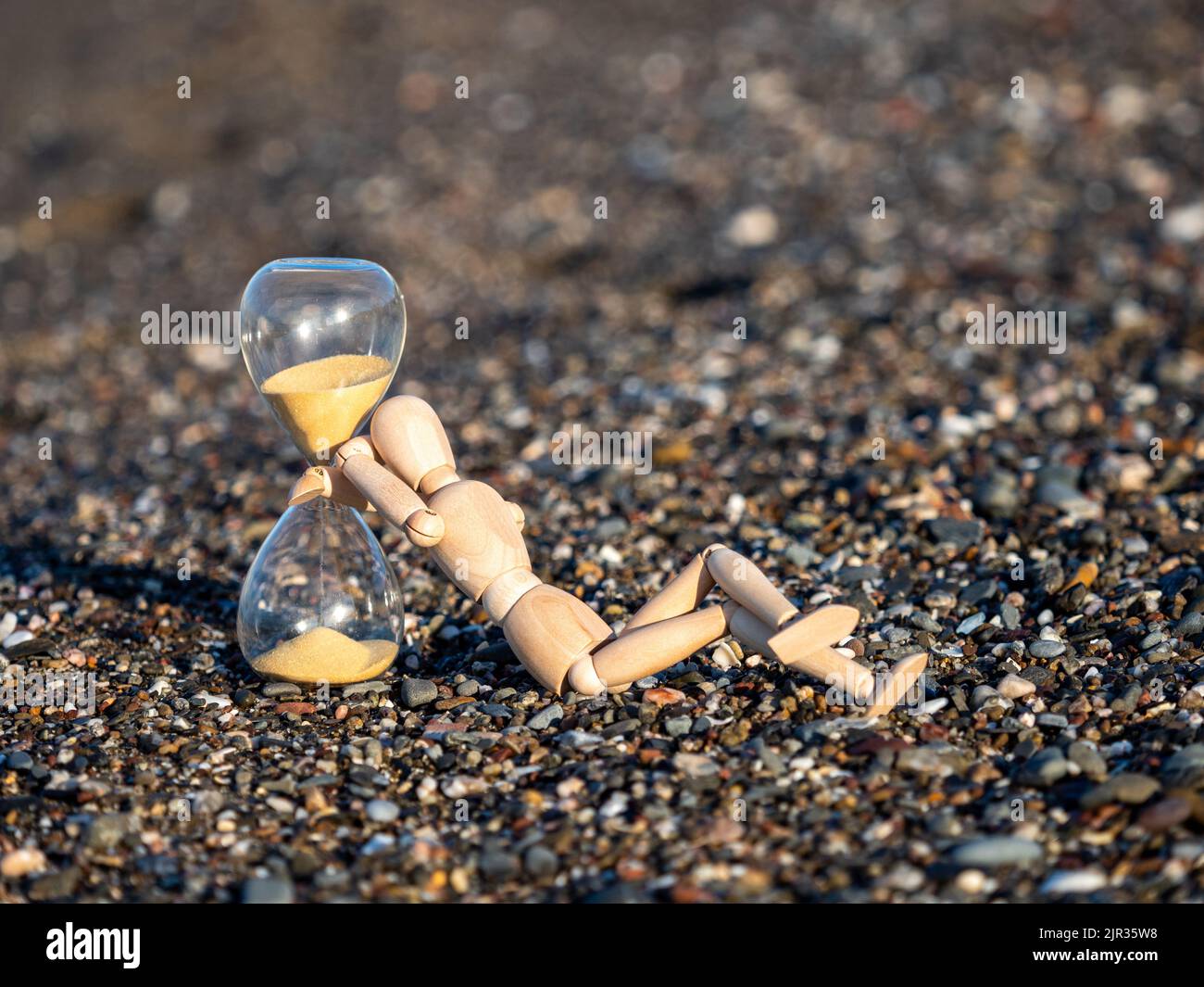 Wooden stick figure next to hourglass on the beach at the seashore ...