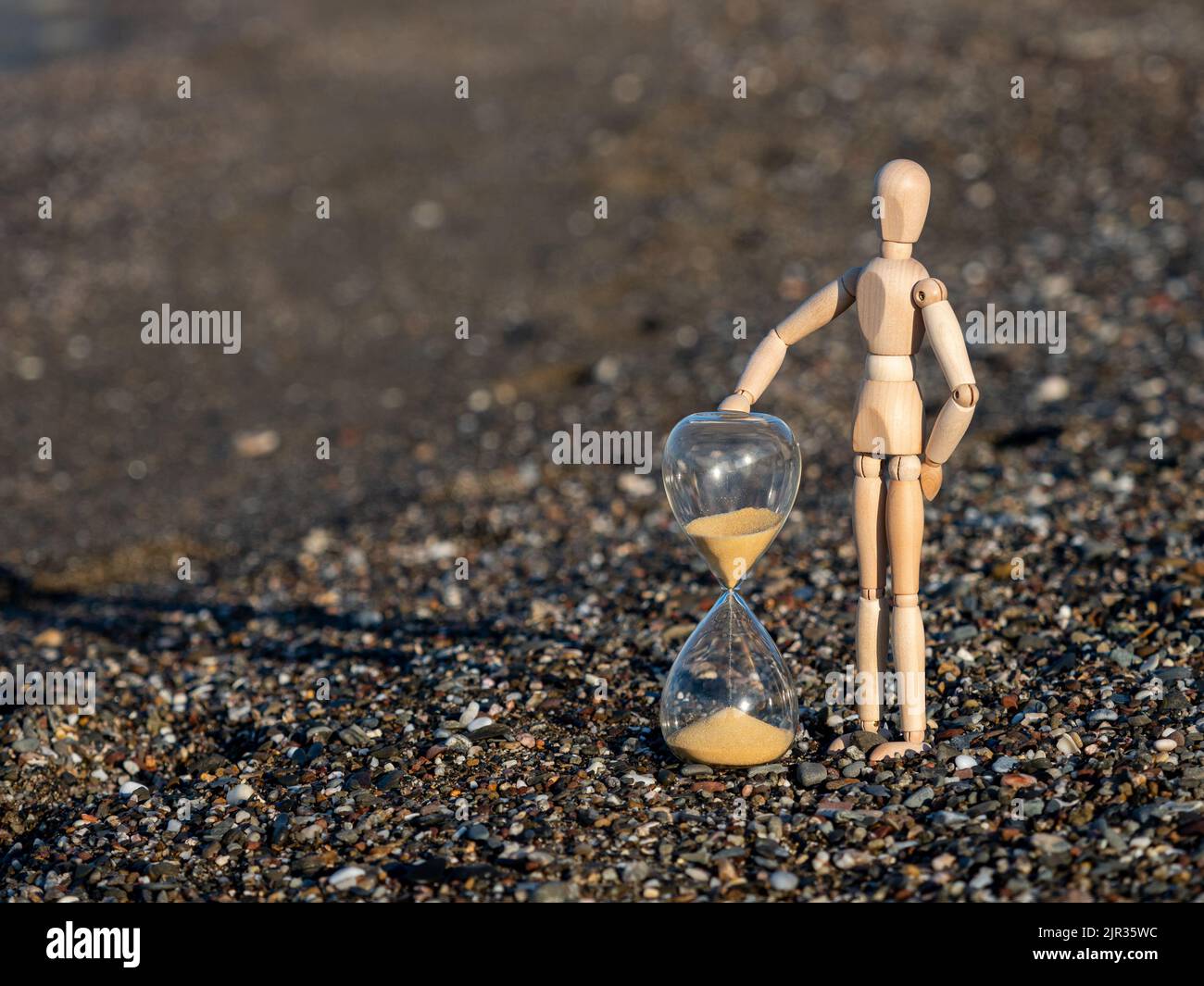 Wooden stick figure next to hourglass on the beach at the seashore ...