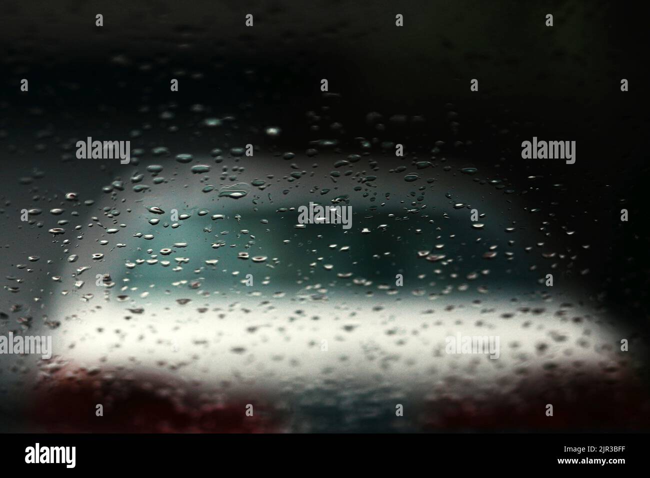 A rainy view of water droplets on the rear windscreen of an old car ...