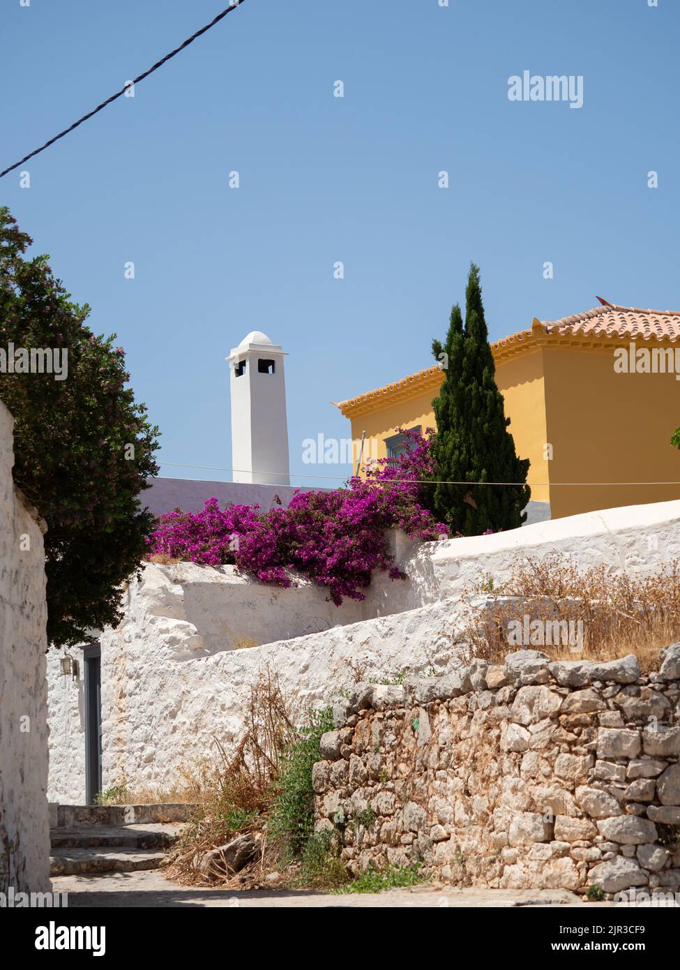 Villa in Greek village, yellow house surrounded by white walls and pink ...