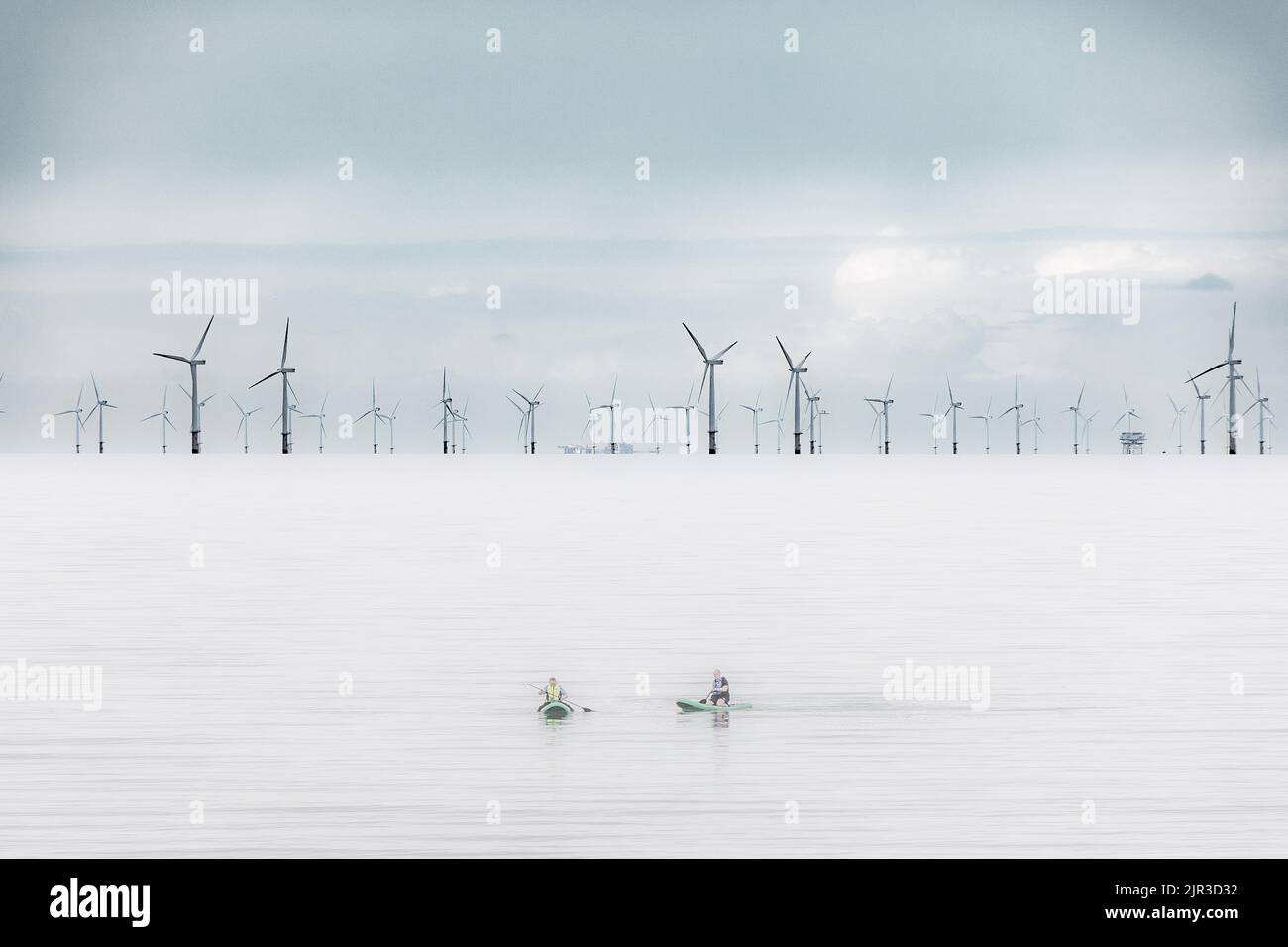 2 men in canoes in the sea with a wind farm on the horizon Stock Photo ...