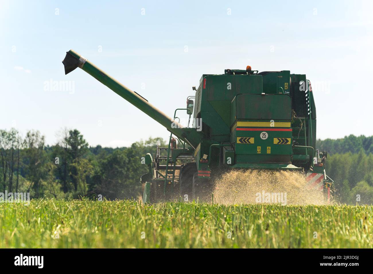 Back-view of a modern green combine working on the field. Forest and ...