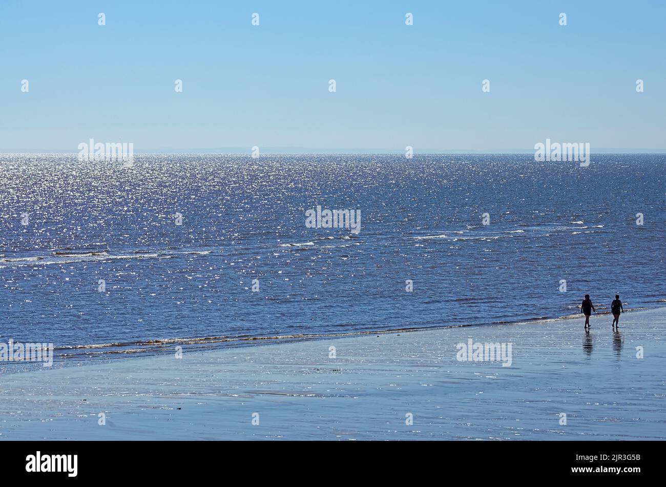 sea front with the Norfolk coast on the horizon and two people walking ...