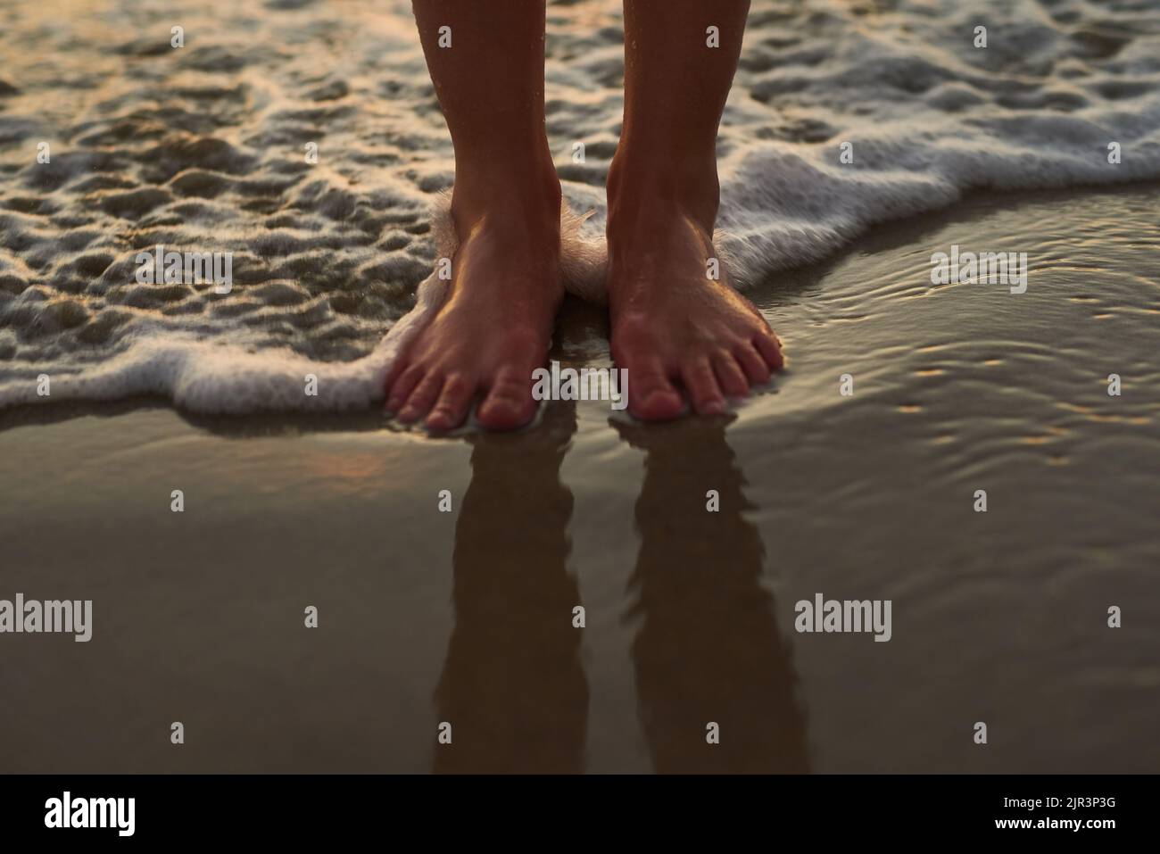 Testing the waters. a woman standing with her feet in the water Stock ...