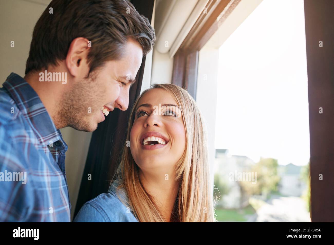 Love and laughter. an affectionate young couple standing at a window in ...