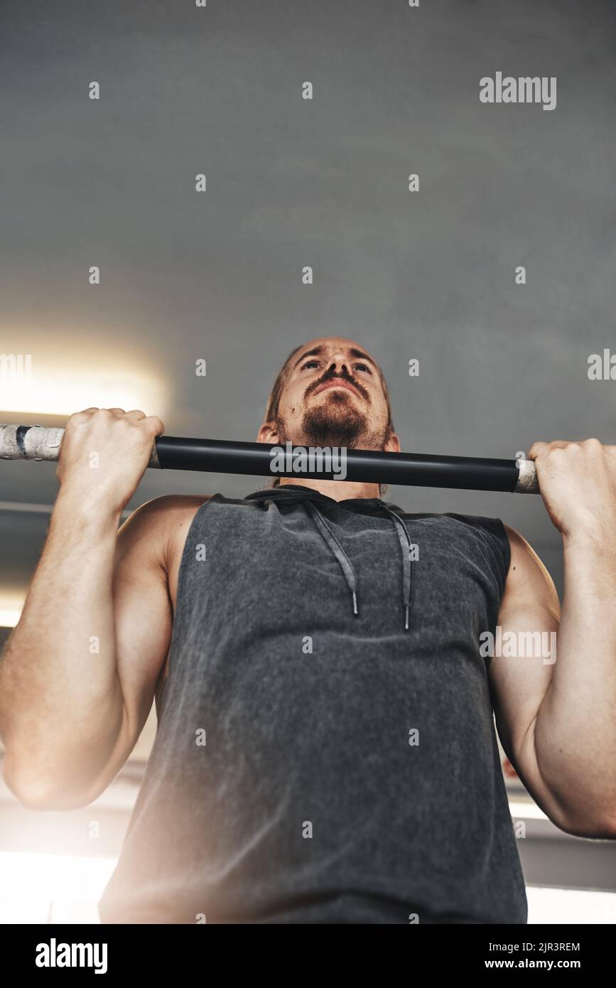 Working on his upper body strength. a young man doing pull ups in a gym ...