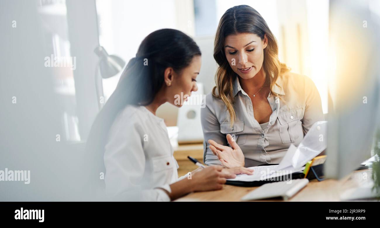 Please sign here. two young businesswomen talking to each other while ...
