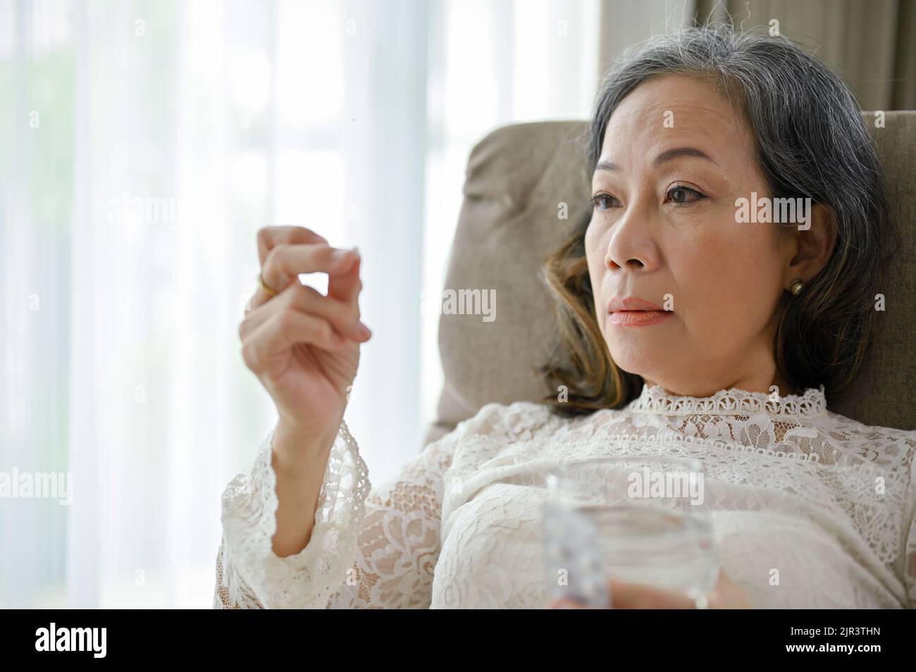 A stressed and depressed Asian middle-aged woman takes a medicine or ...