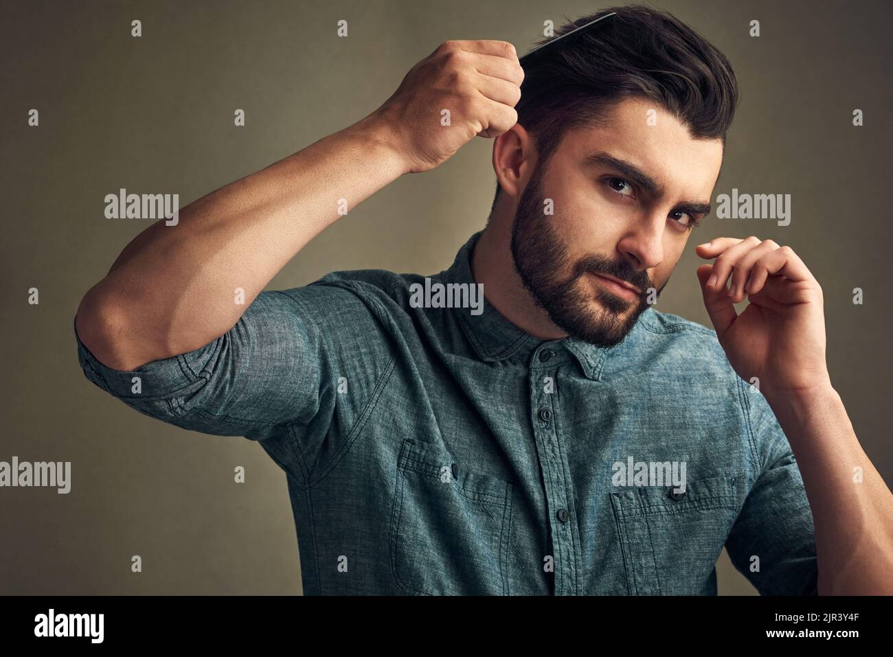 Beard season is here. Studio shot of a handsome young man combing his ...