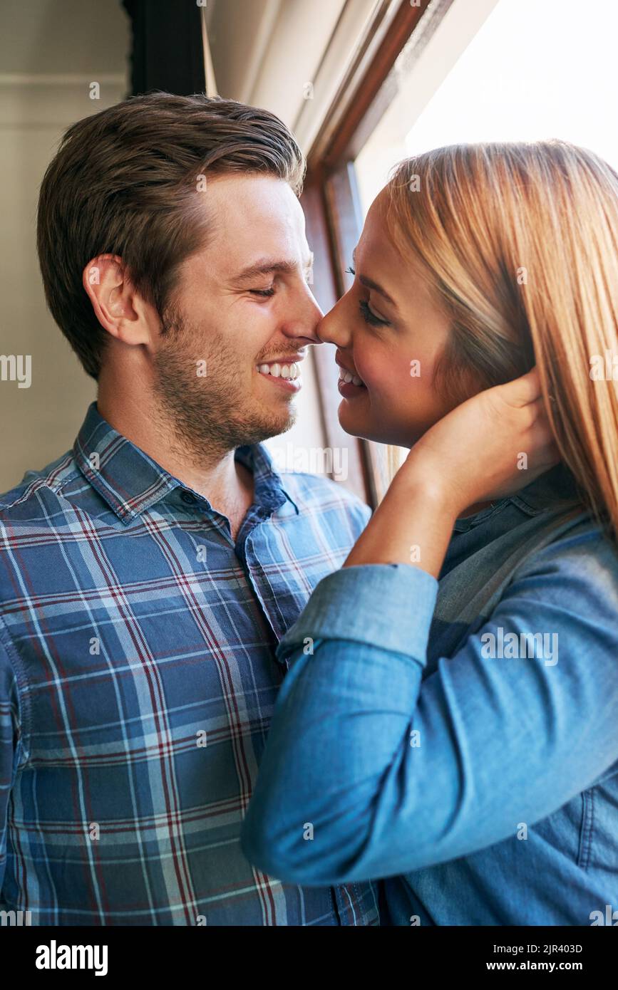 Kiss me. an affectionate young couple standing at a window in their ...
