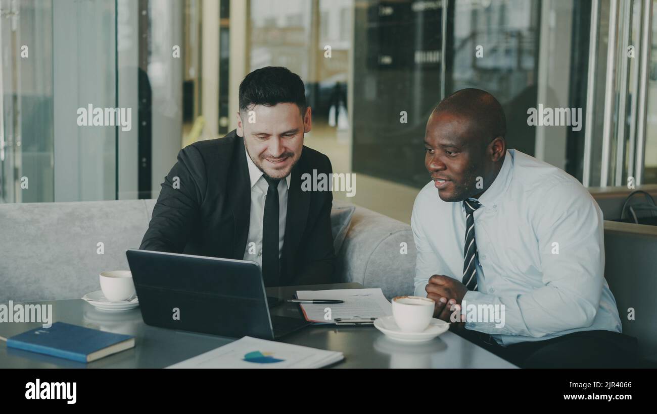 Two multi ethnic businessmen looking at laptop computer and laughing in ...