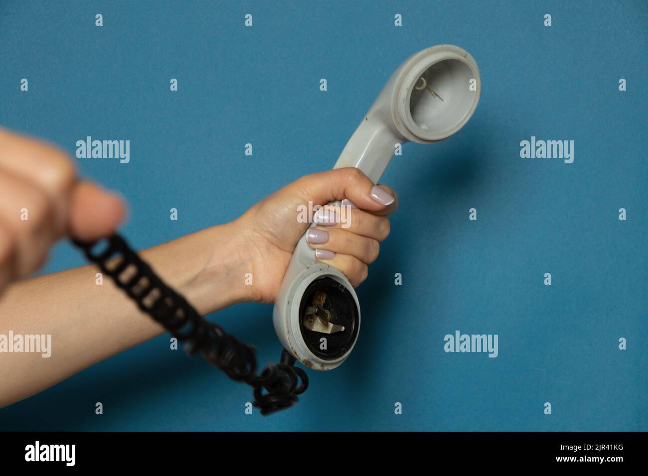 female hand holding an old broken telephone receiver on a wire on a ...