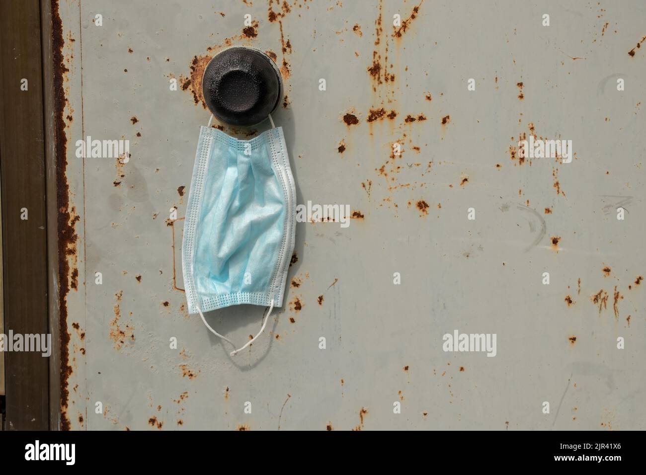a medical mask hangs on the handle on an old iron rusty door on the ...