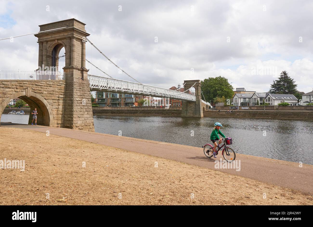 Child cycling along a river path near a footbridge in Nottingham, UK ...