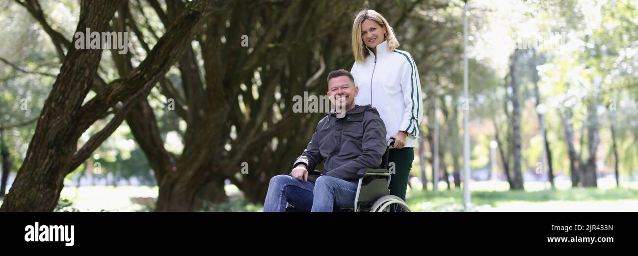Woman on walk in park with man in wheelchair Stock Photo - Alamy