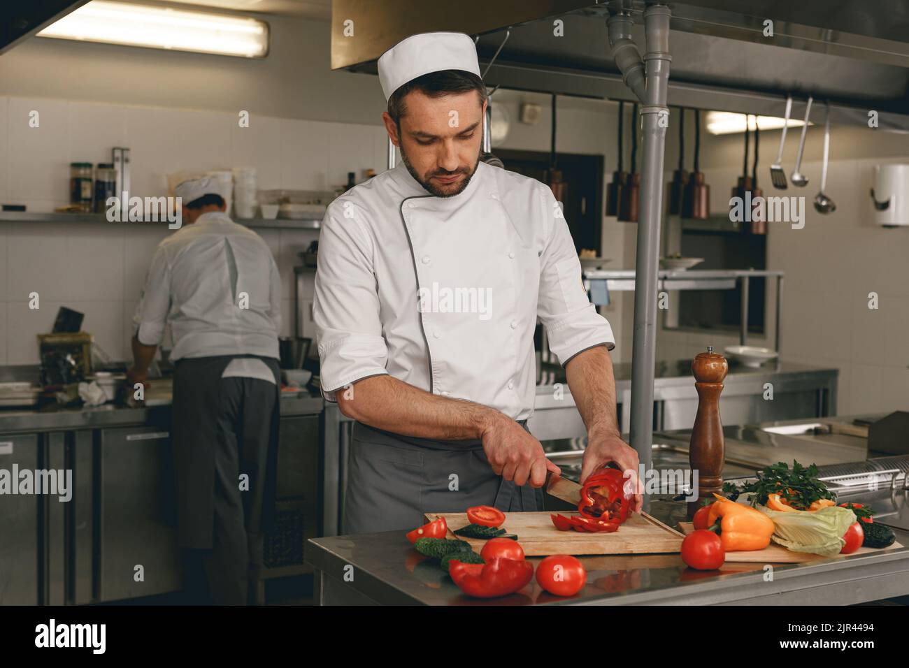 Busy chef cutting red pepper and cucumbers on a board for making salad ...