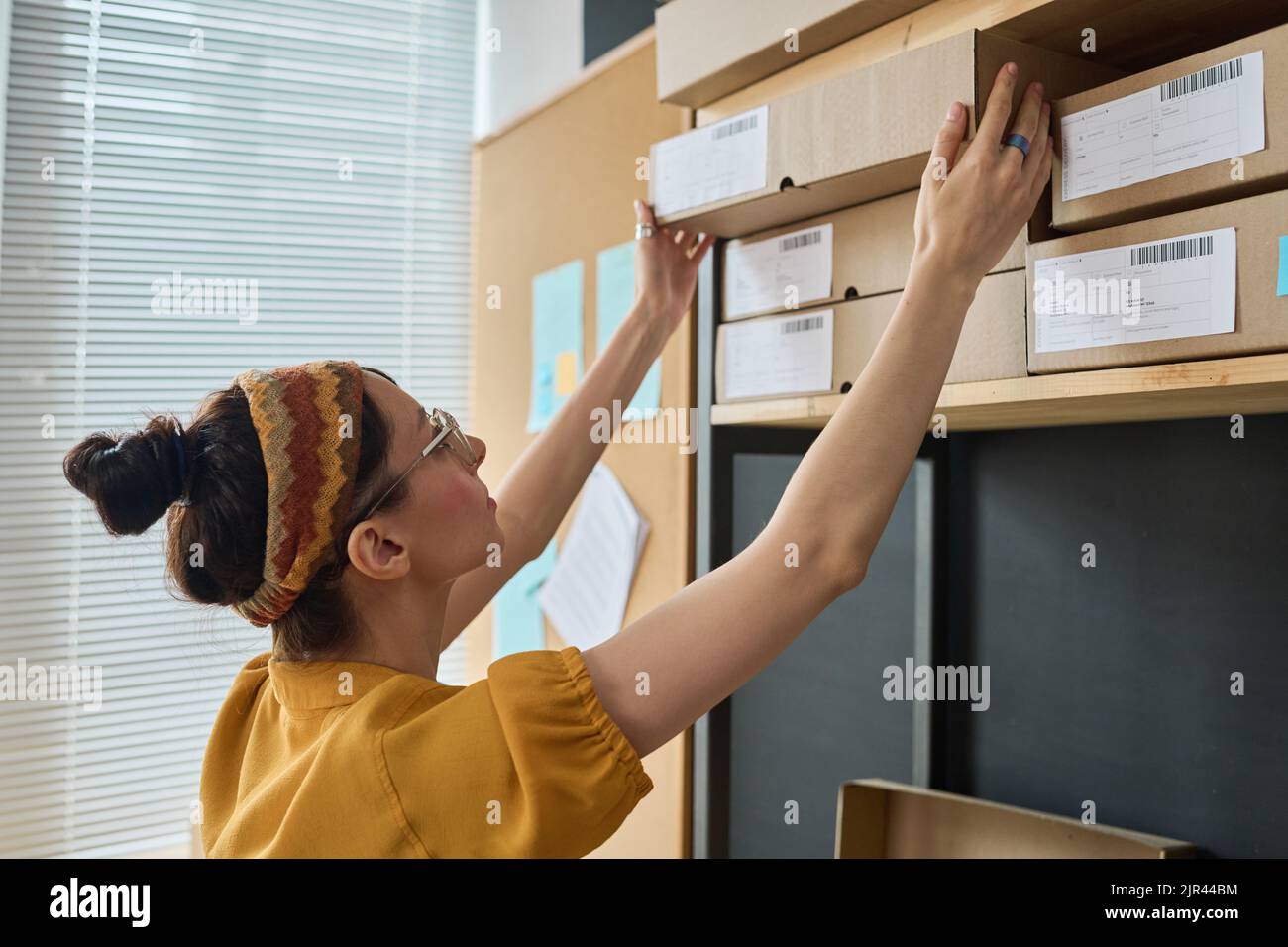 Young woman taking parcel in cardboard box from the shelf for ...