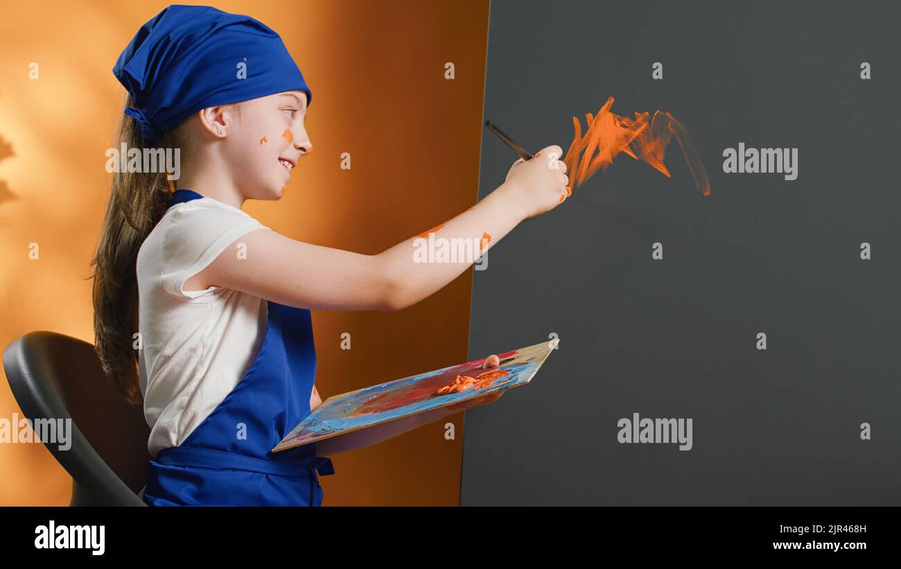 Small girl using paintbrush to create art masterpiece on canvas ...