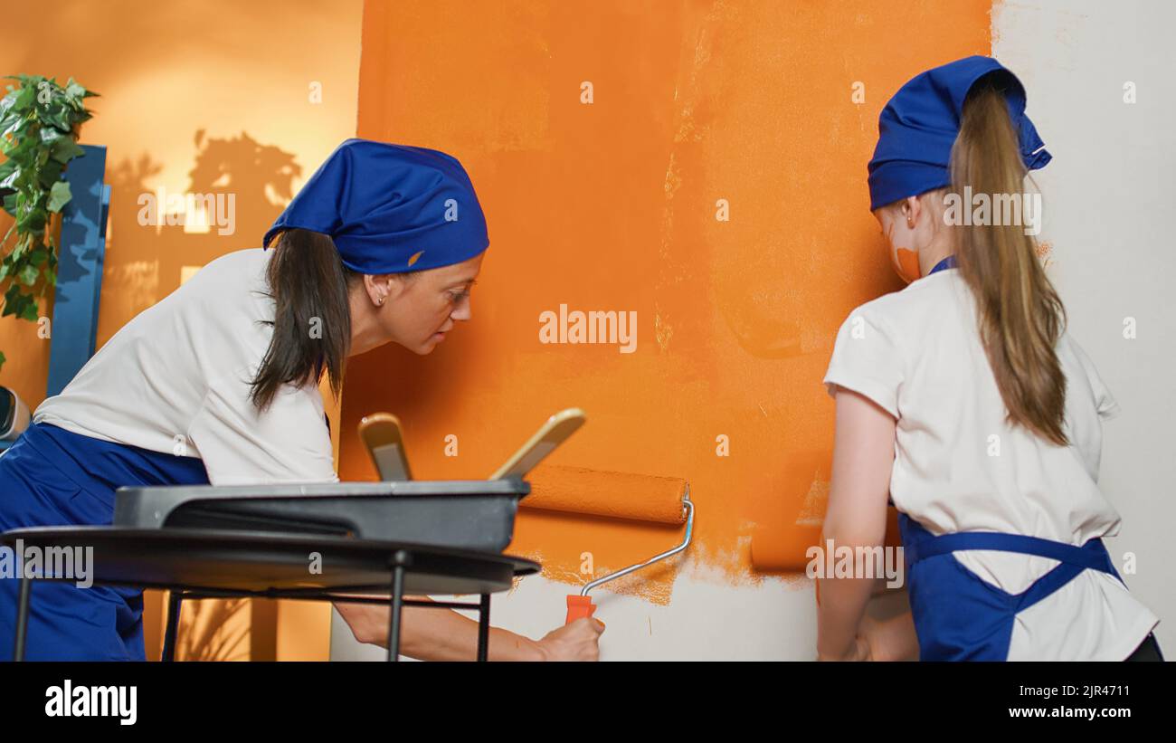 Young people using orange paint and roller brush on walls, renovating ...