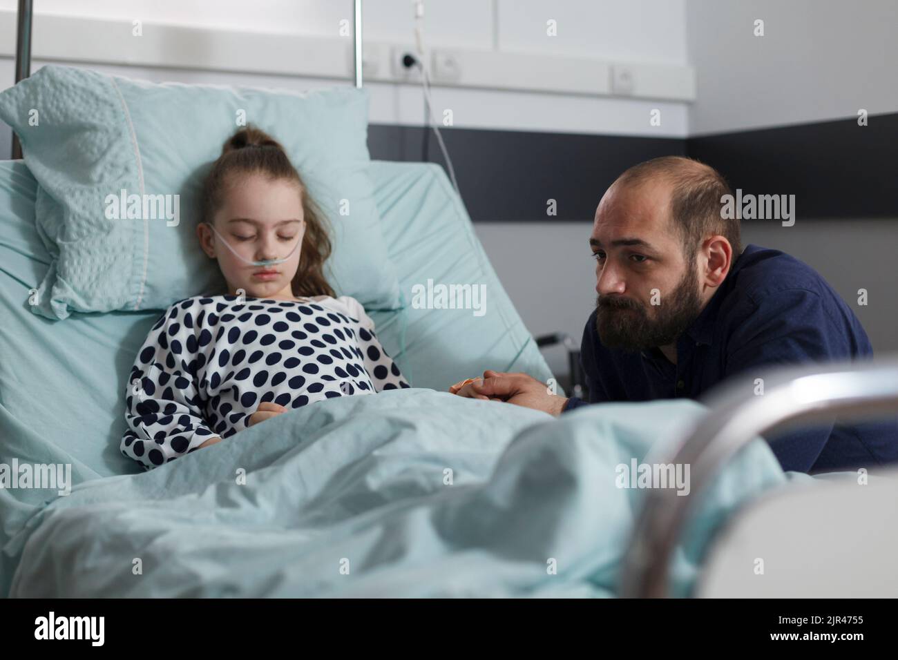 Sad father sitting beside hospitalized sick girl resting on patient bed ...