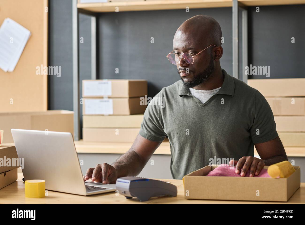 African serious man packing order in box and typing data of parcel in ...