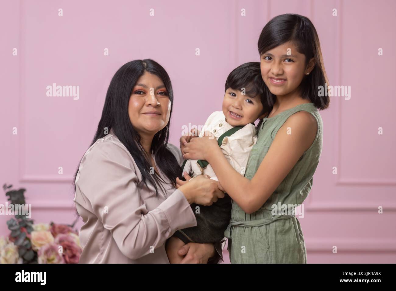 A Hispanic mother with her two children hugging on a pink background ...