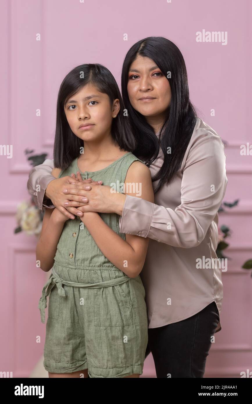 A vertical of Hispanic mother with her daughter hugging on a pink ...