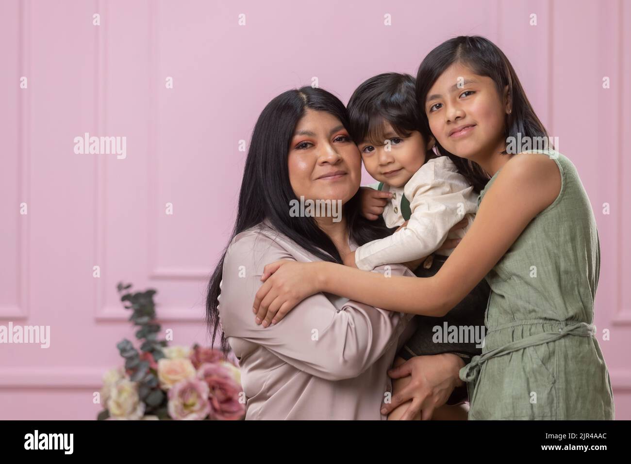 A Hispanic mother with her two children hugging on a pink background ...