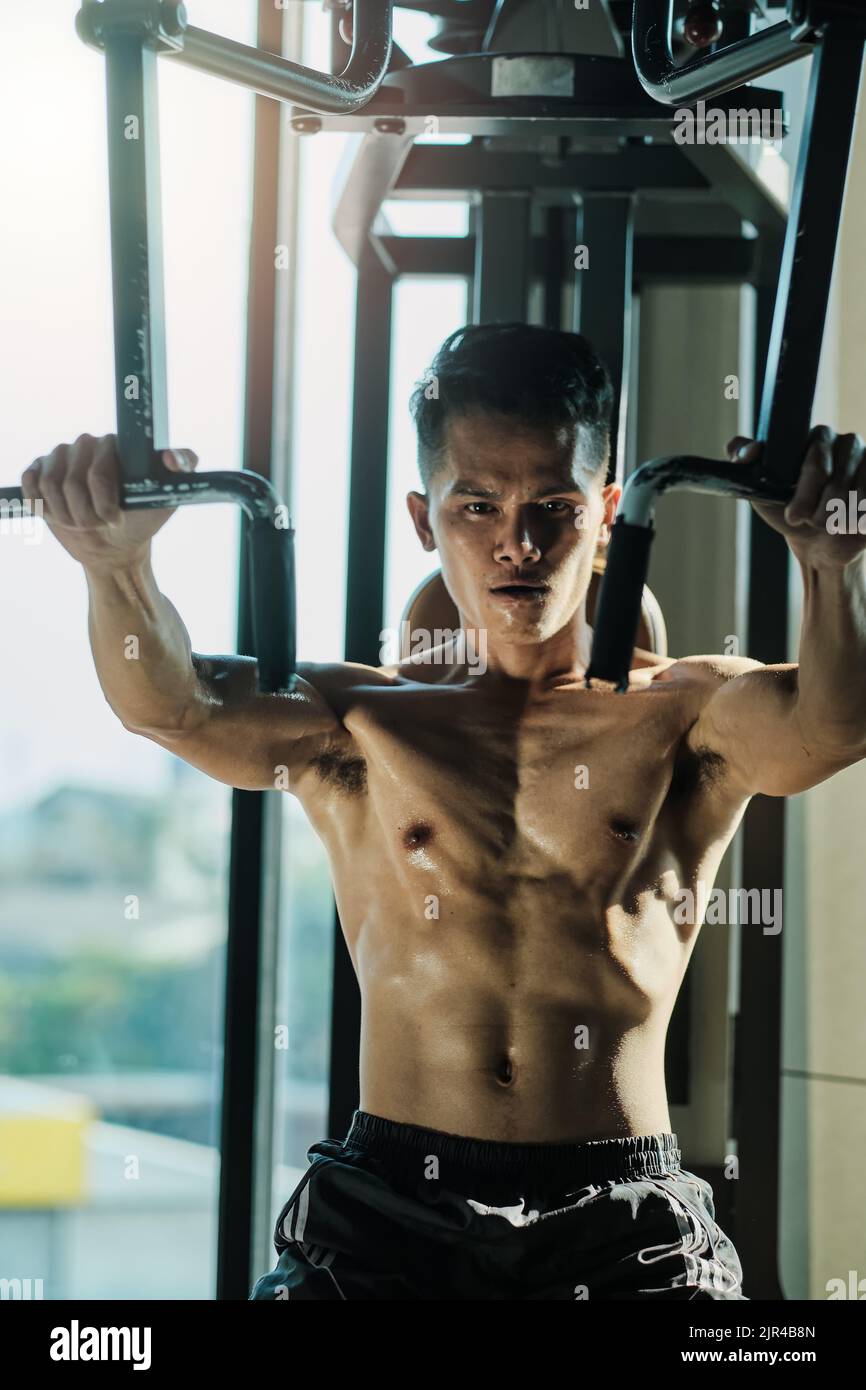 A vertical of a young South East Asian man working out in a gym using a ...