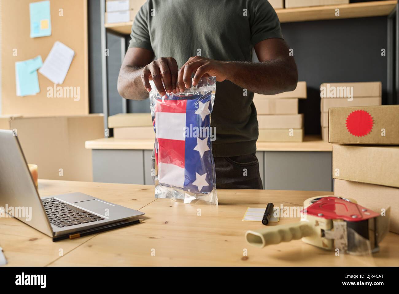Close-up of African man packing American flag in packet at table and ...
