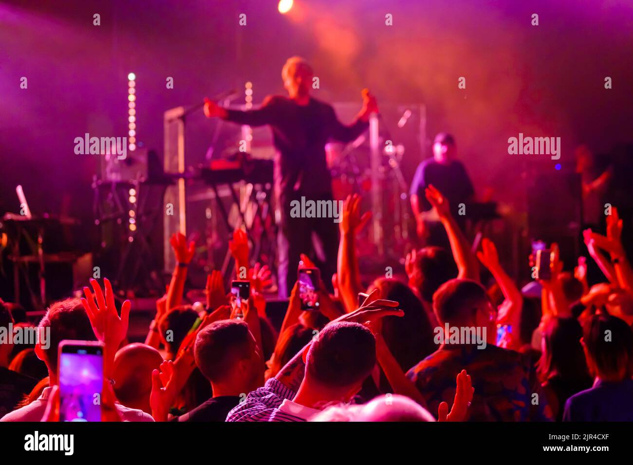 Anonymous people raising arms and dancing under red neon illumination ...