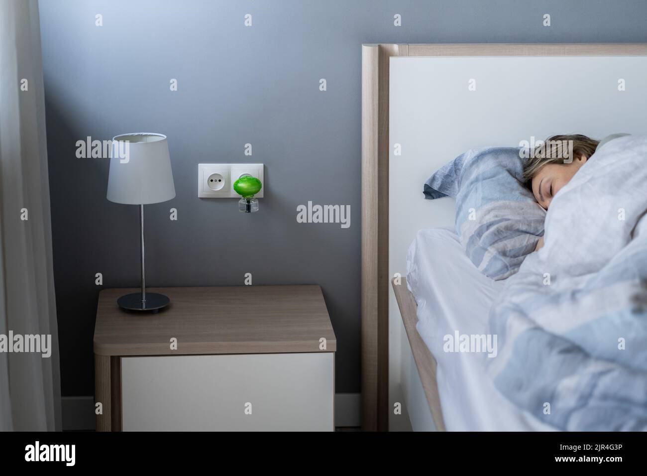 Female sleep in bed next to an electric fumigator in socket to protect ...