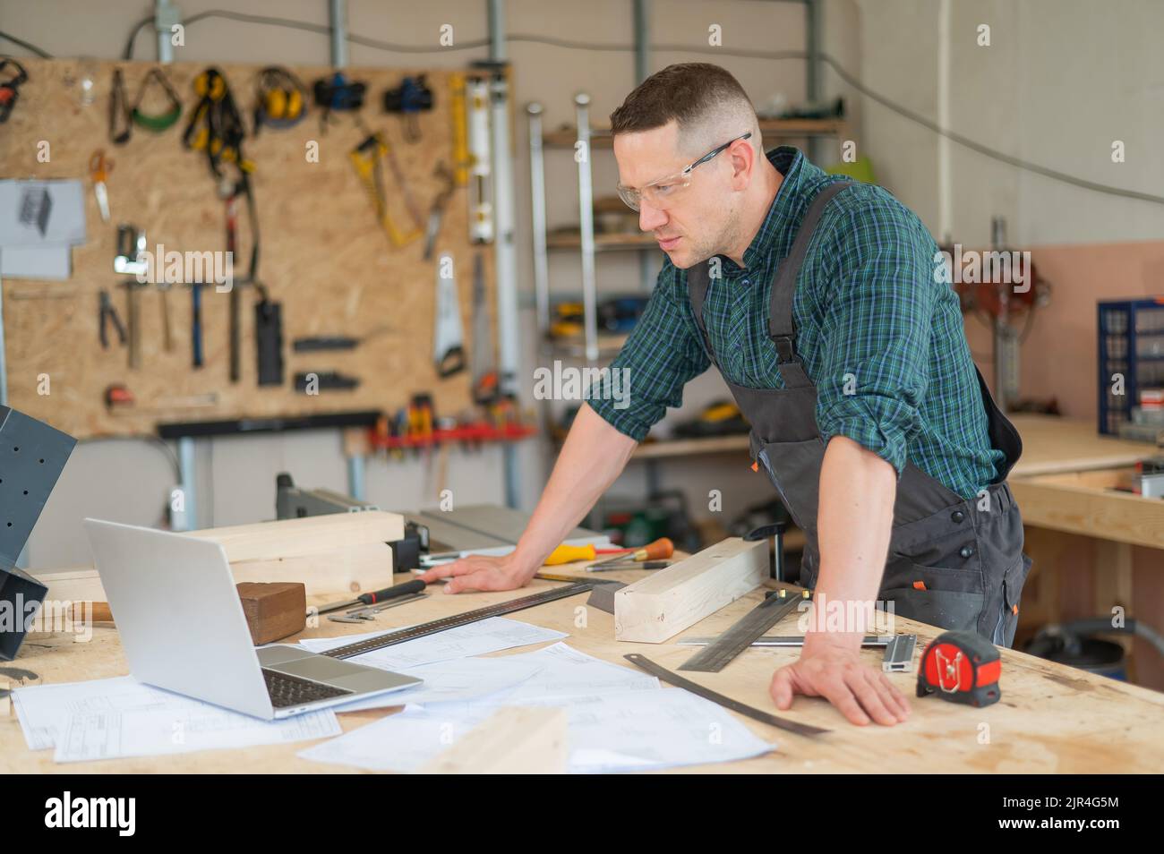 Portrait of a carpenter in protective glasses and work overalls uses a ...