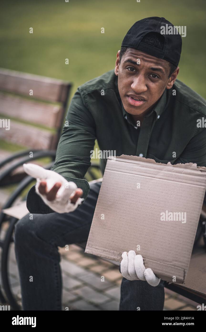 Man sitting on bench holding out hand to camera Stock Photo - Alamy