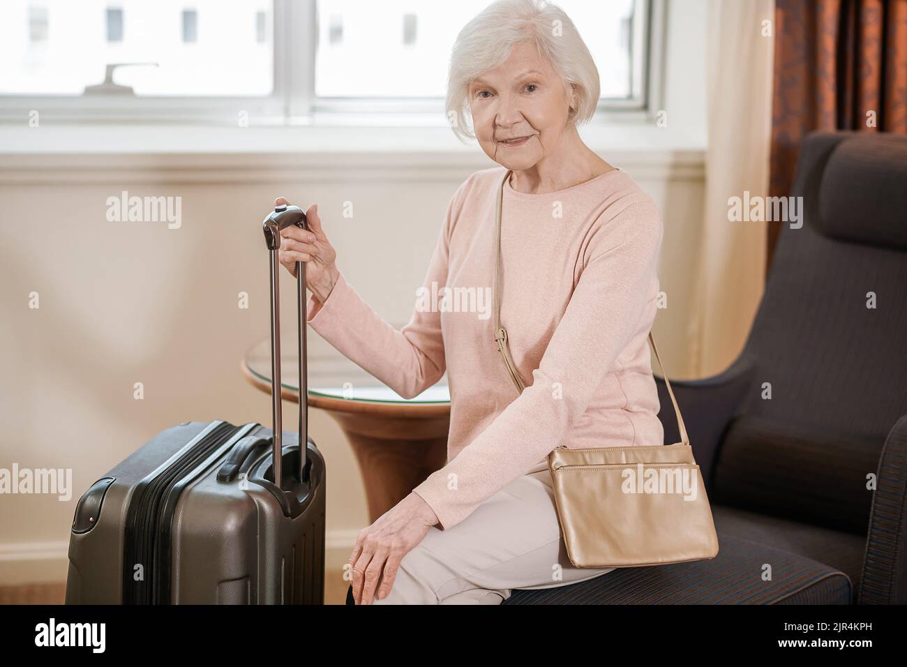 Good-looking senior woman sitting with a suitcase in a hotel room Stock ...