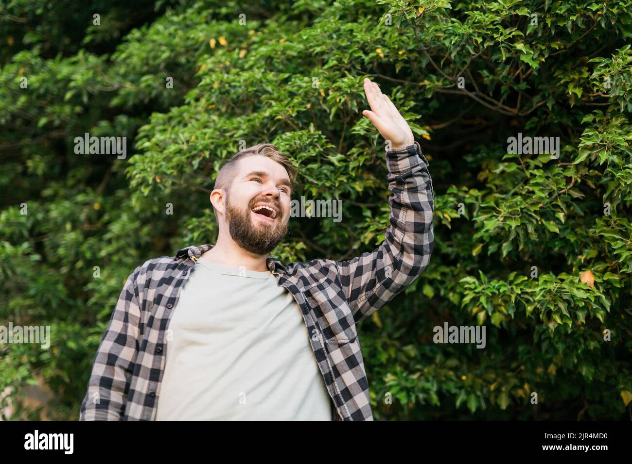 Side view of delighted male standing outdoors and waving hand to his ...