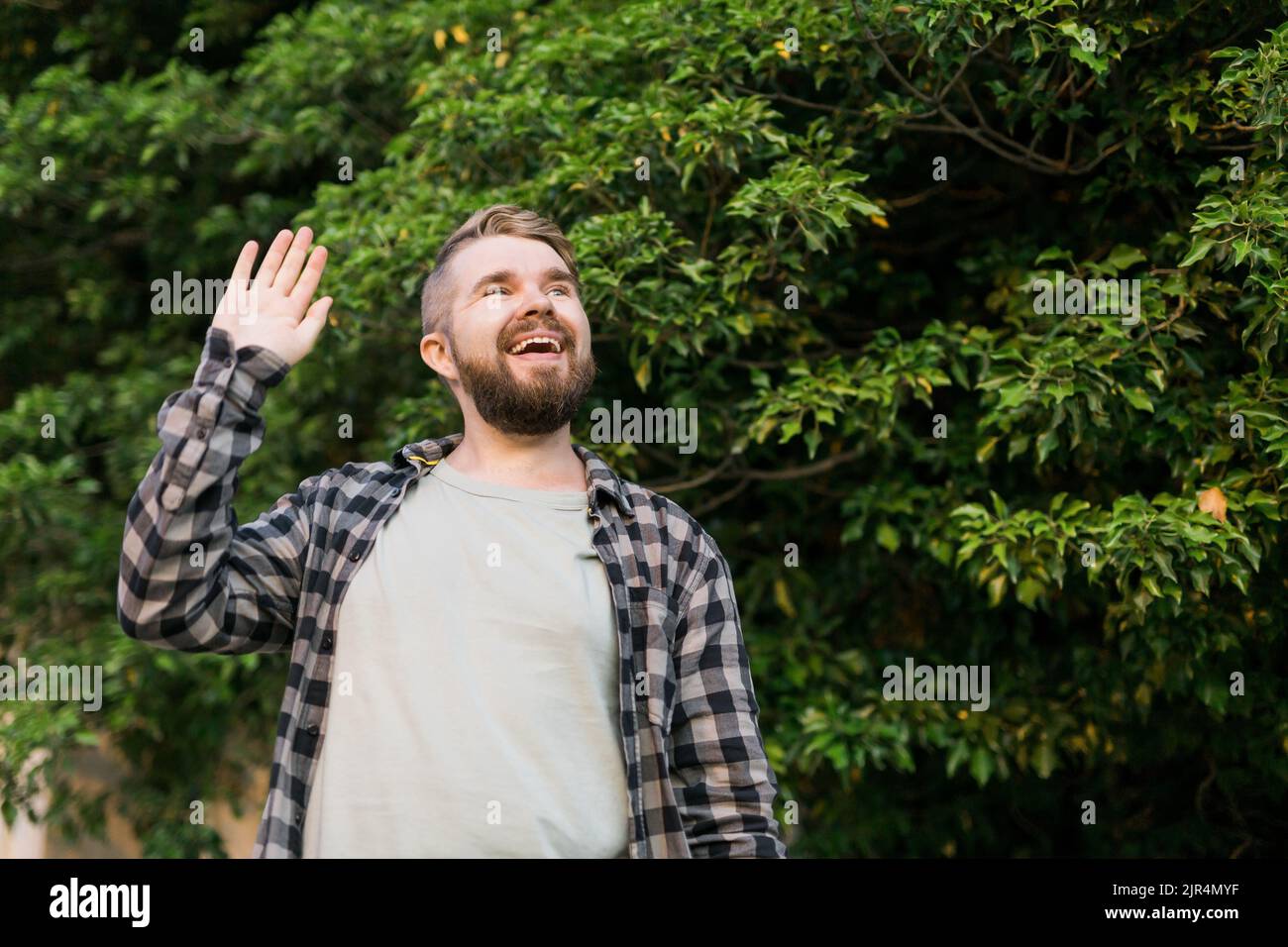 Side view of delighted male standing outdoors and waving hand to his ...