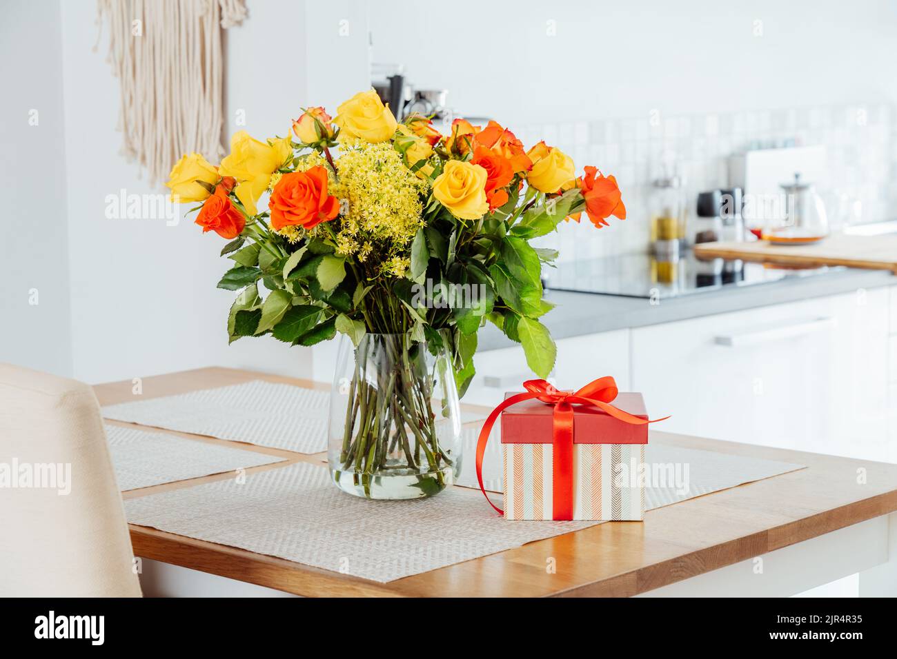 Yellow and orange roses in a vase and gift box with red ribbon on ...