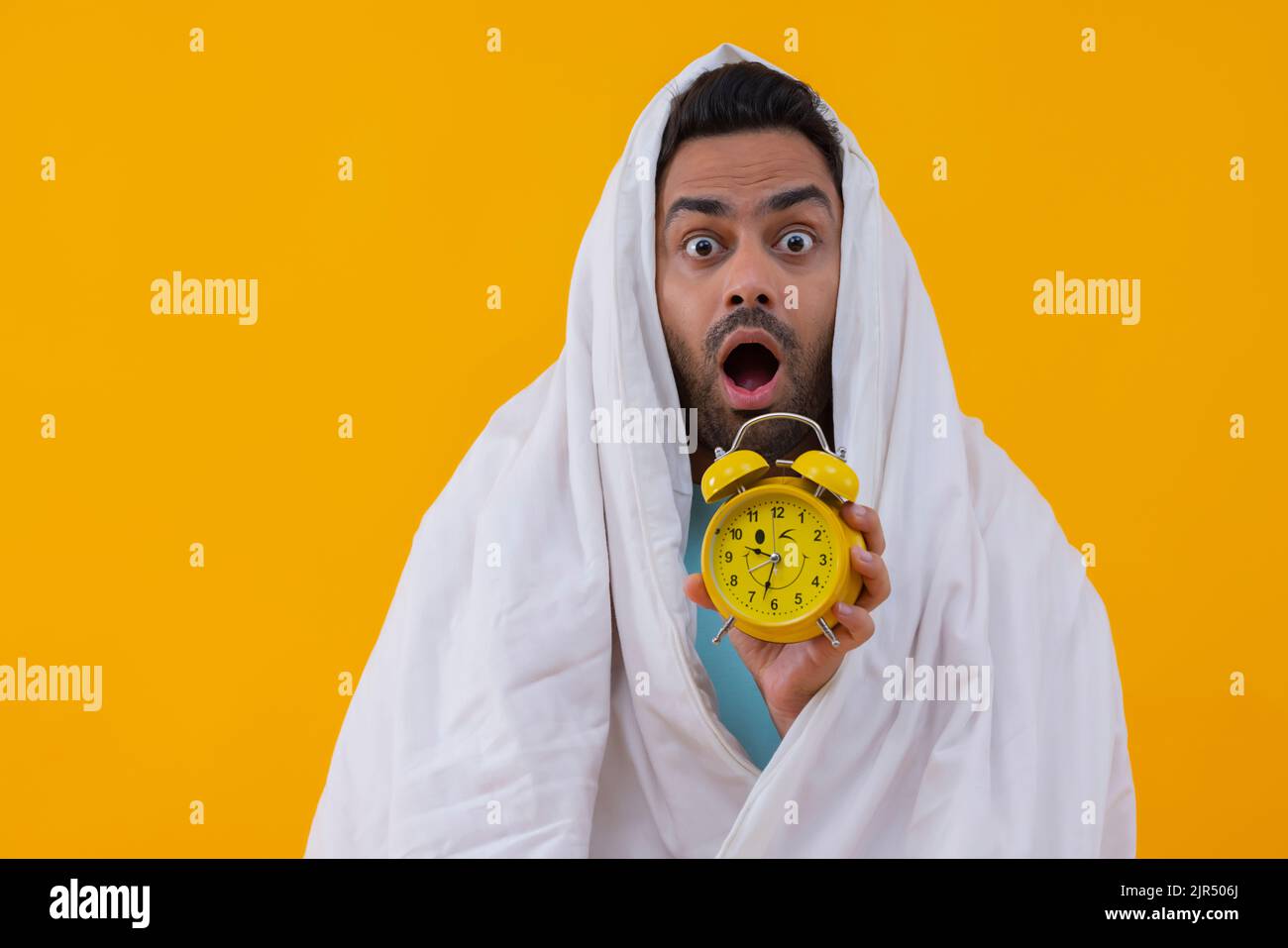 Portrait of a shocked young man holding alarm clock over yellow ...
